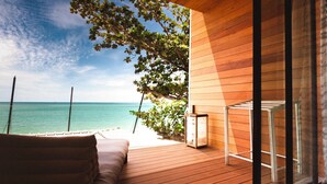 Um deck de madeira com vista para o oceano, uma porta de vidro e uma pequena mesa.