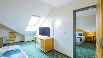 Quarto de hotel com cama, escrivaninha com computador, cadeira, abajur e claraboia.