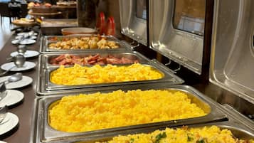 Buffet com diversas opções de comida, incluindo ovos mexidos, pão de milho e carnes.