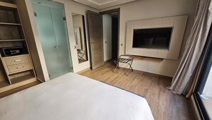 Quarto de hotel com cama, guarda-roupa, espelho, televisão e uma pequena mesa.