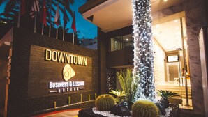 Entrada de um hotel com uma placa indicando "DOWNTOWN BUSINESS & LEISURE HOTELS" e uma fonte decorativa na frente.
