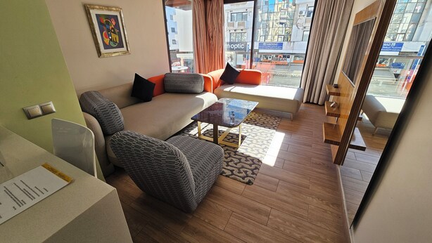 Uma sala de estar moderna com um sofá, poltronas, uma mesa de centro e vista para a cidade através de grandes janelas.