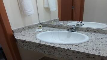 Um banheiro com duas pias brancas, bancada de granito e espelho sobre as pias.