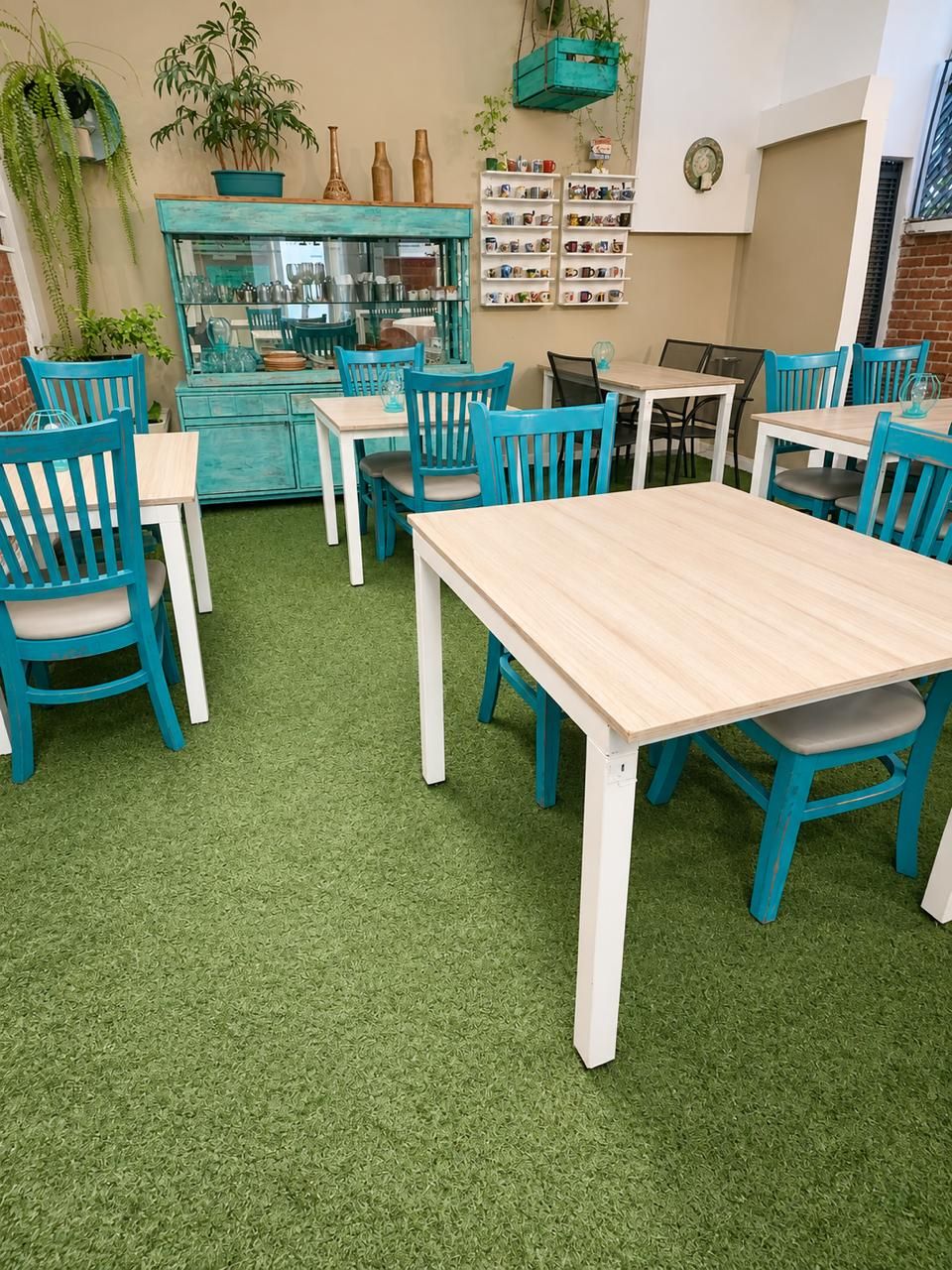 Quarto com cadeiras verde-água e mesa de madeira, cercado por grama sintética verde.