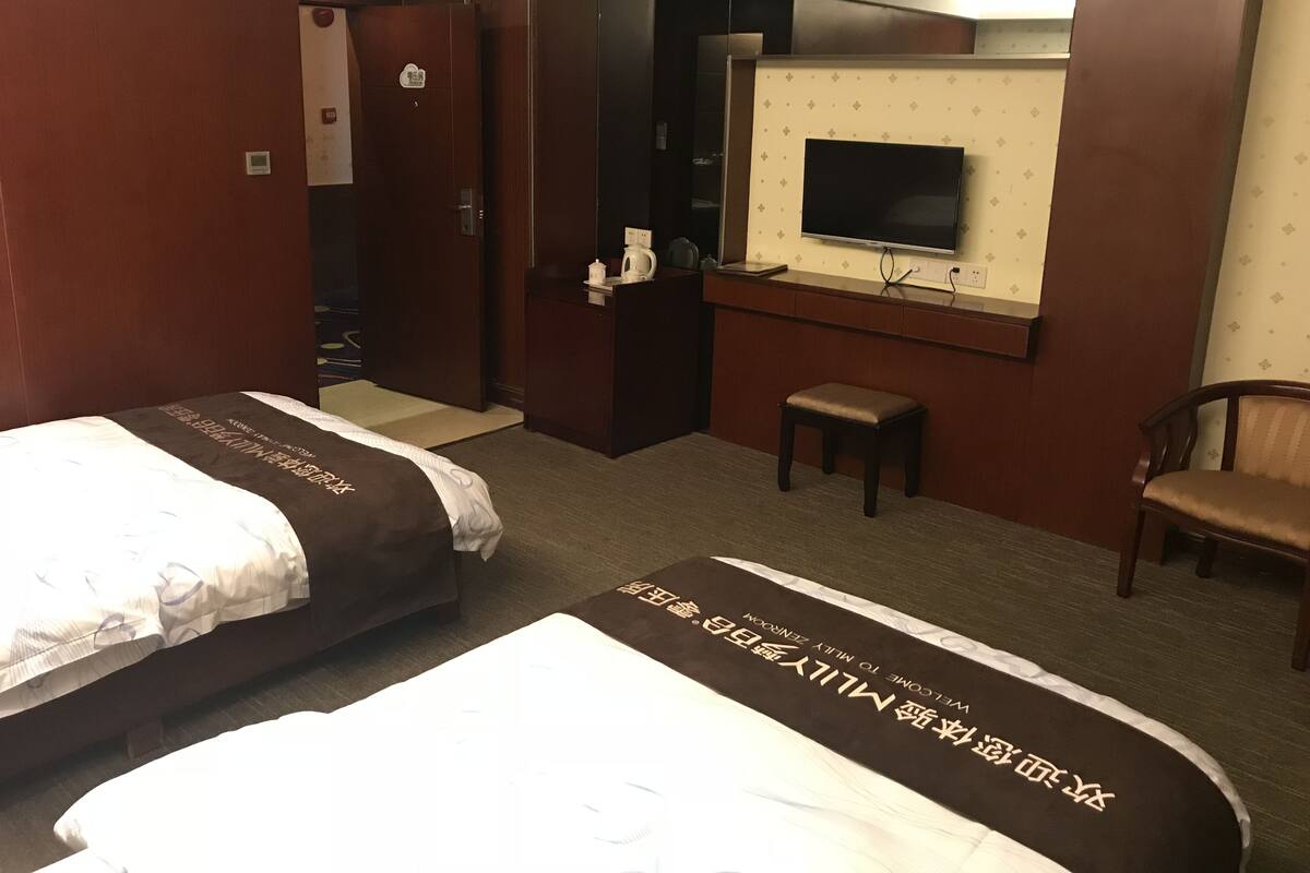 Quarto de hotel com duas camas, uma mesa, uma televisão e uma cadeira.