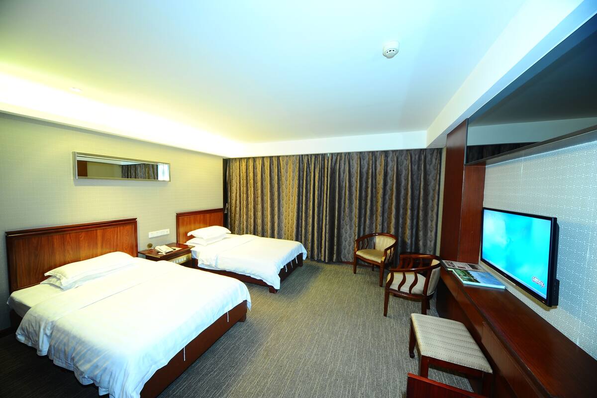 Quarto de hotel com duas camas, uma escrivaninha com computador, uma cadeira, uma televisão e um espelho na parede.