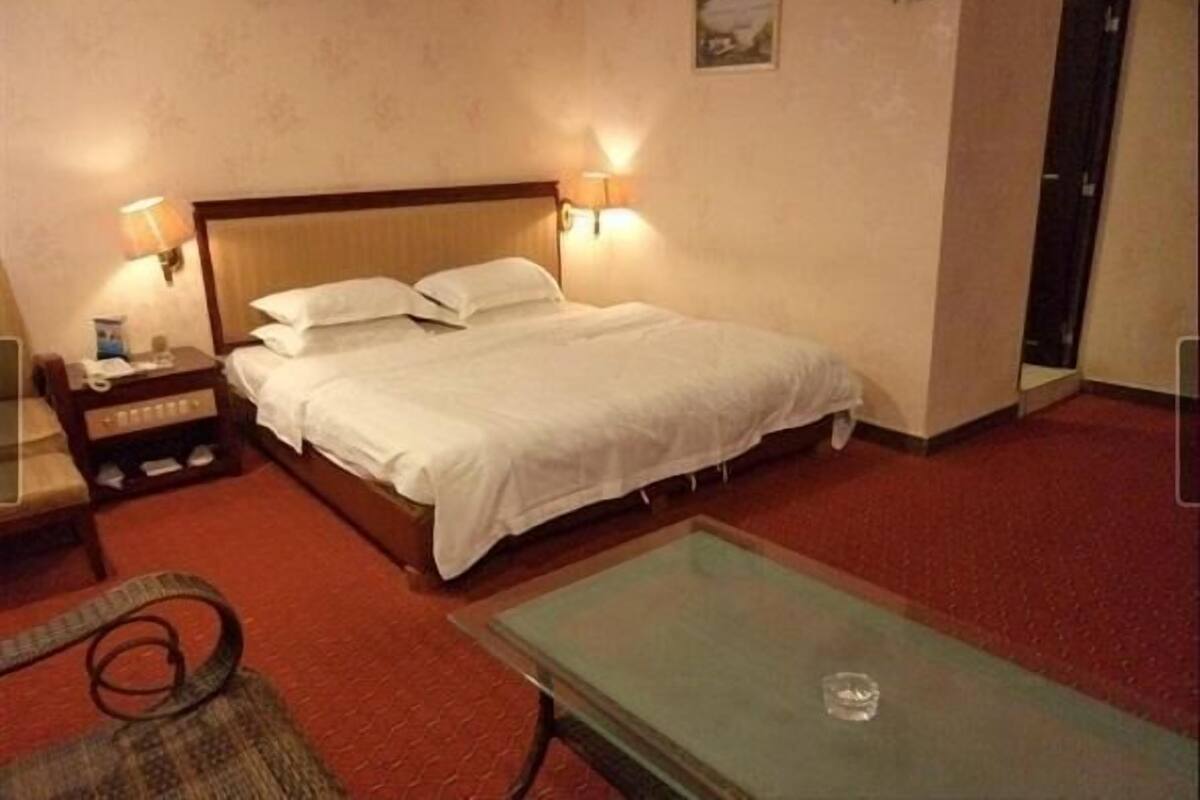 Quarto de hotel com cama, abajures, uma mesinha e uma cadeira.