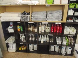 Um espaço de armazenamento com prateleiras contendo toalhas dobradas, cestos de roupa e diversos artigos domésticos, incluindo garrafas e recipientes.