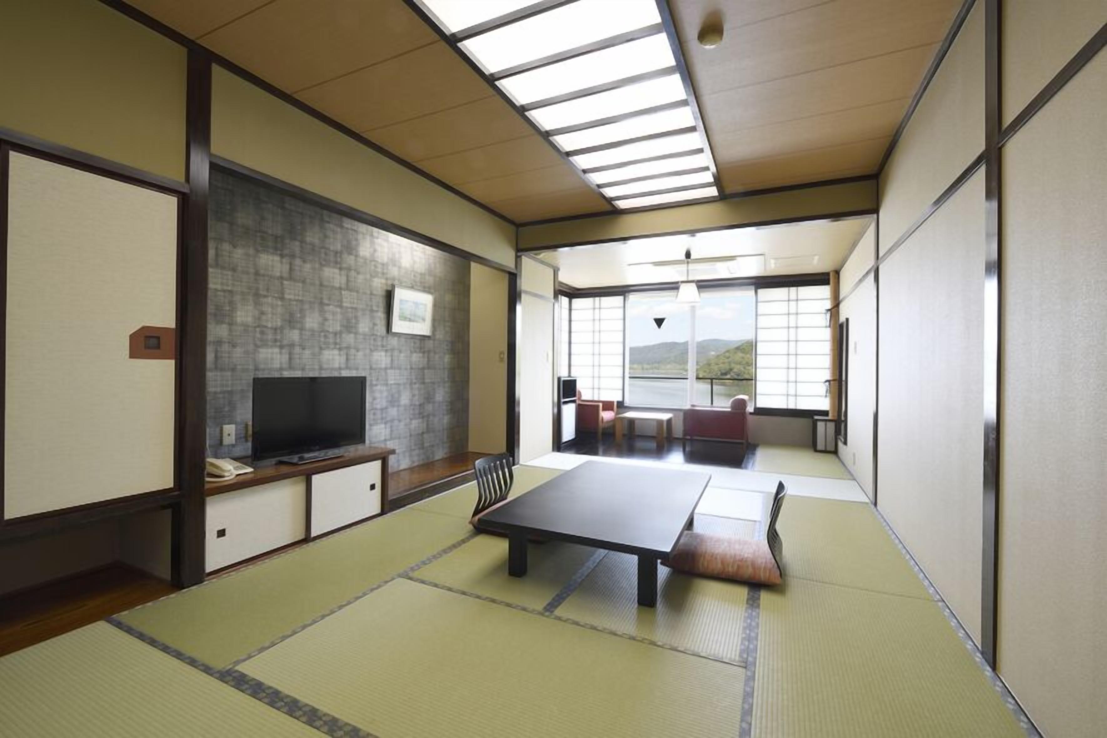 Quarto com esteiras de tatame, televisão, sofá e vista para o exterior.