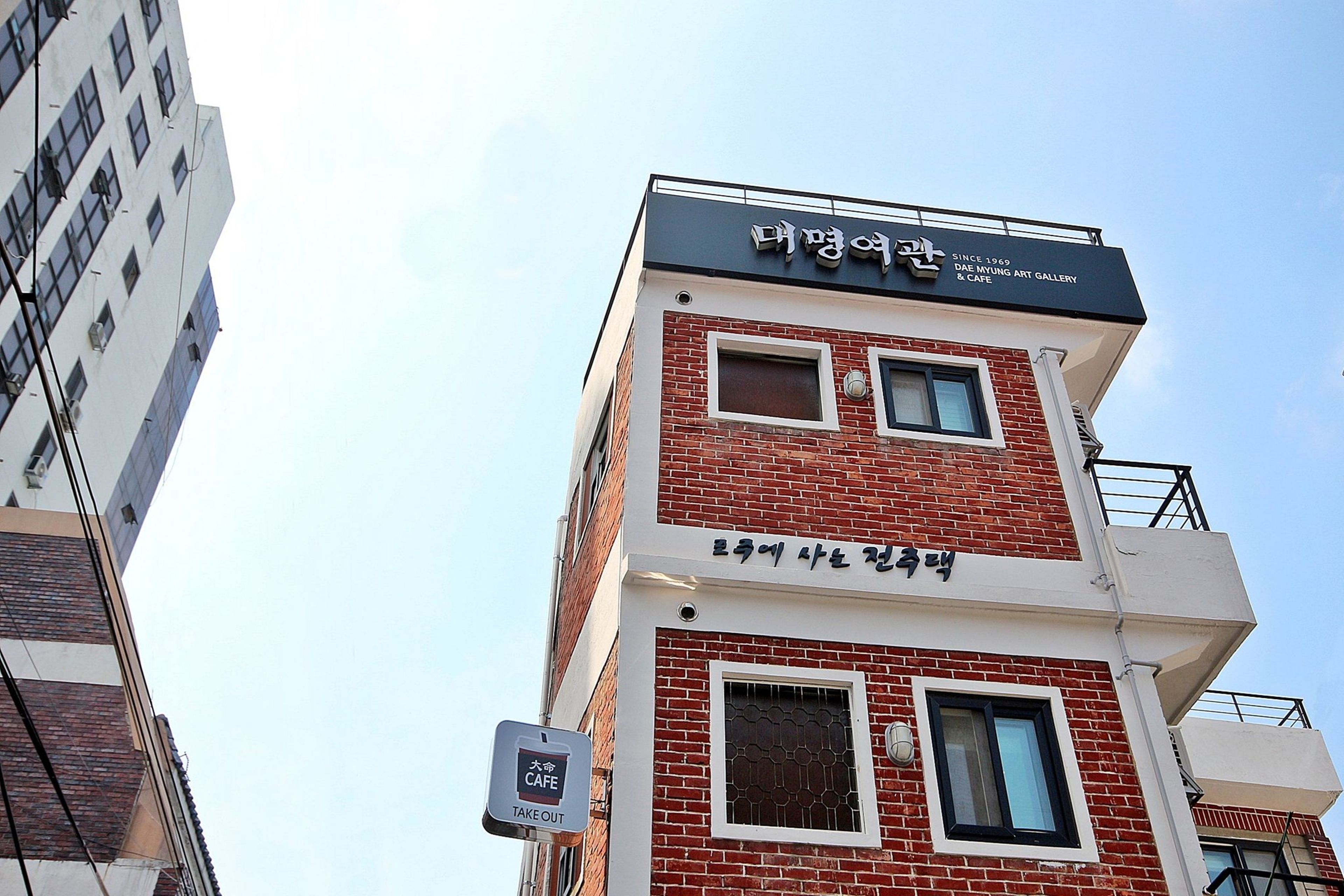Um edifício de vários andares com uma placa para a Galeria de Arte e Café Dae Myung.