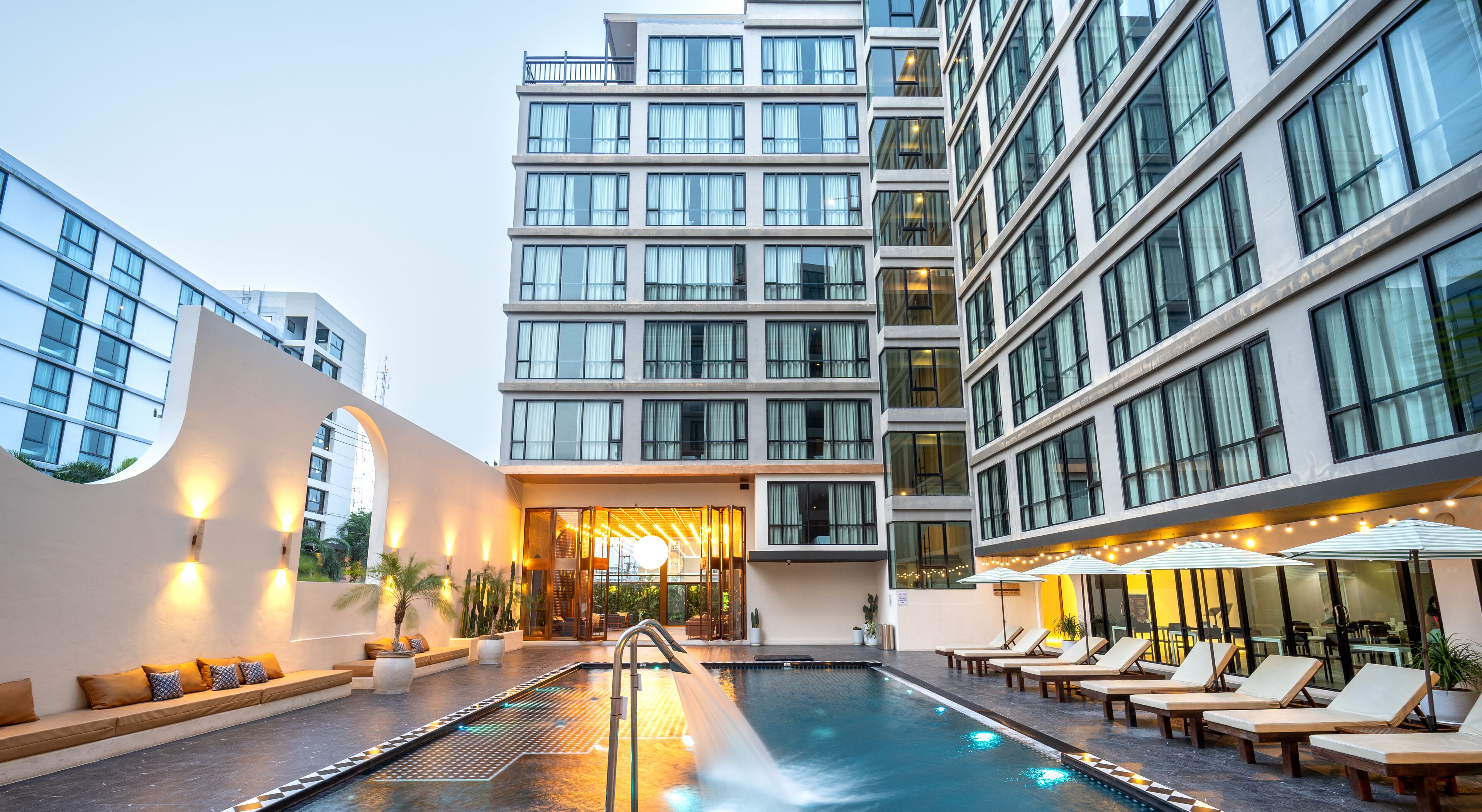 Um hotel moderno com piscina, espreguiçadeiras e entrada bem iluminada.