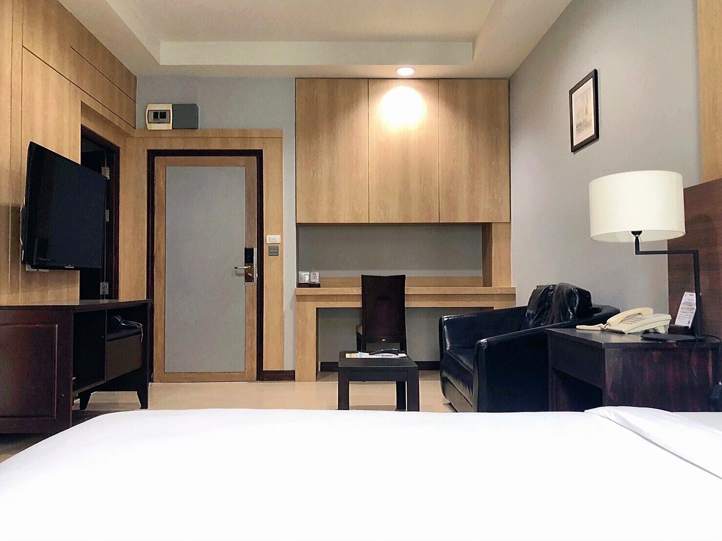 Quarto de hotel com cama, escrivaninha, cadeira, televisão, abajur e telefone.