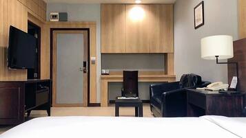 Quarto de hotel com cama, escrivaninha, cadeira, televisão, abajur e telefone.