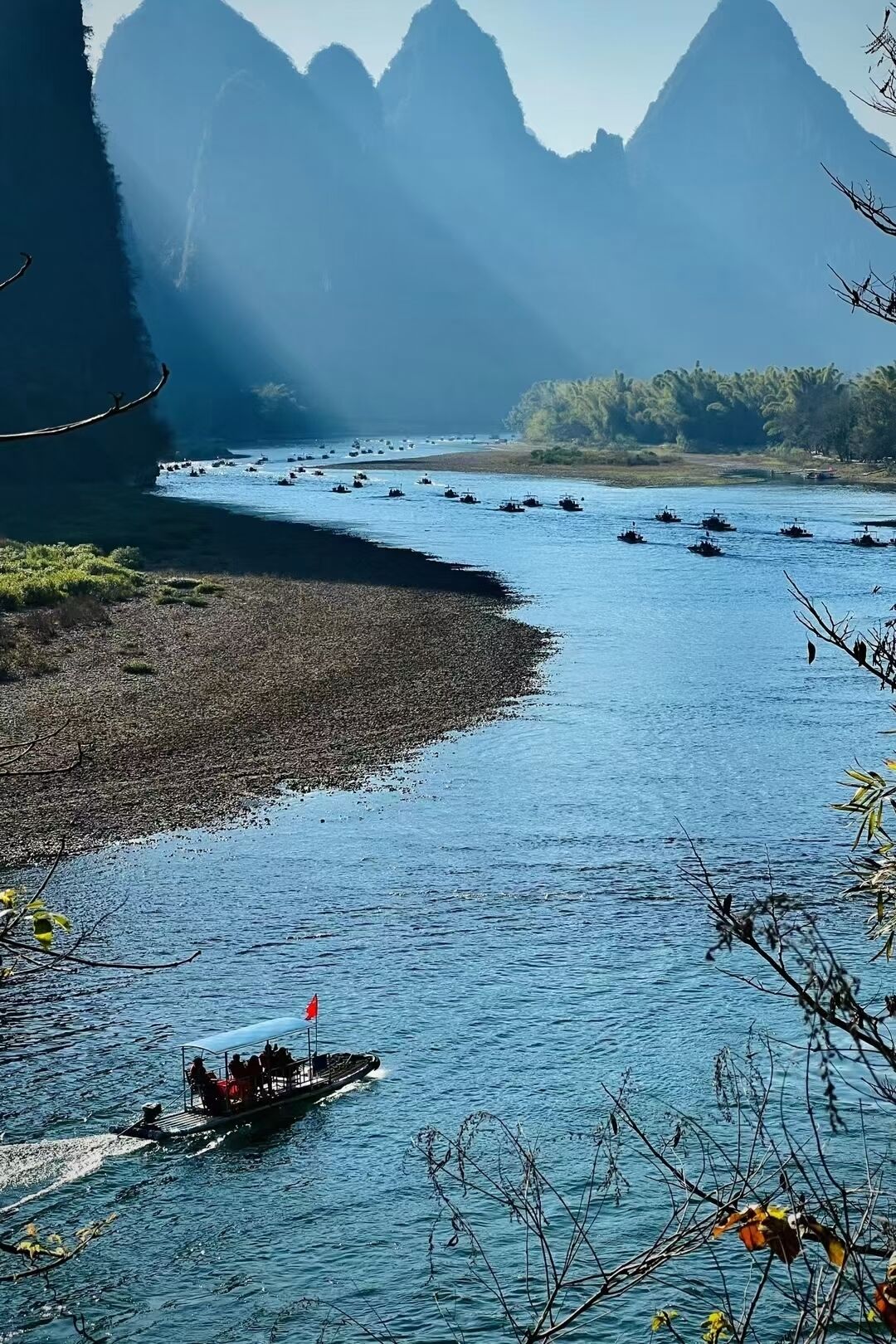 Um rio com barcos, rodeado por montanhas e vegetação.
