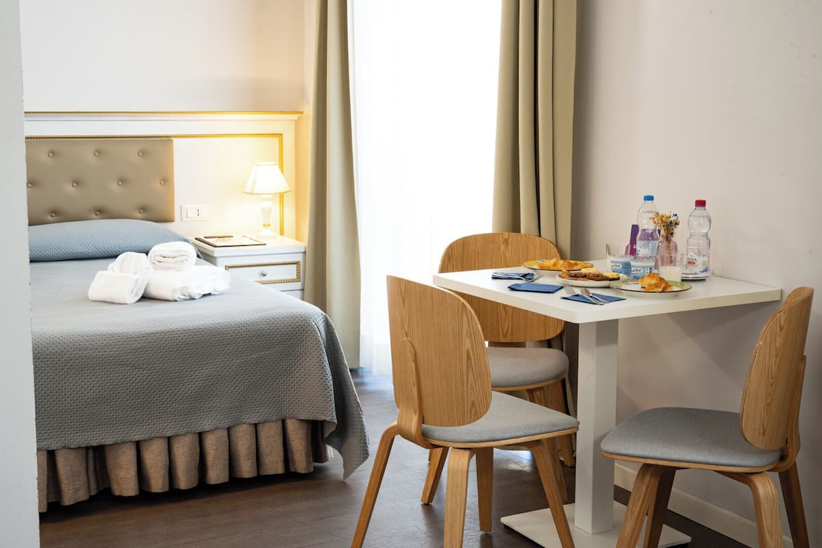 Quarto de hotel com cama, mesa de cabeceira, abajur e mesa de pequeno-almoço com cadeiras.