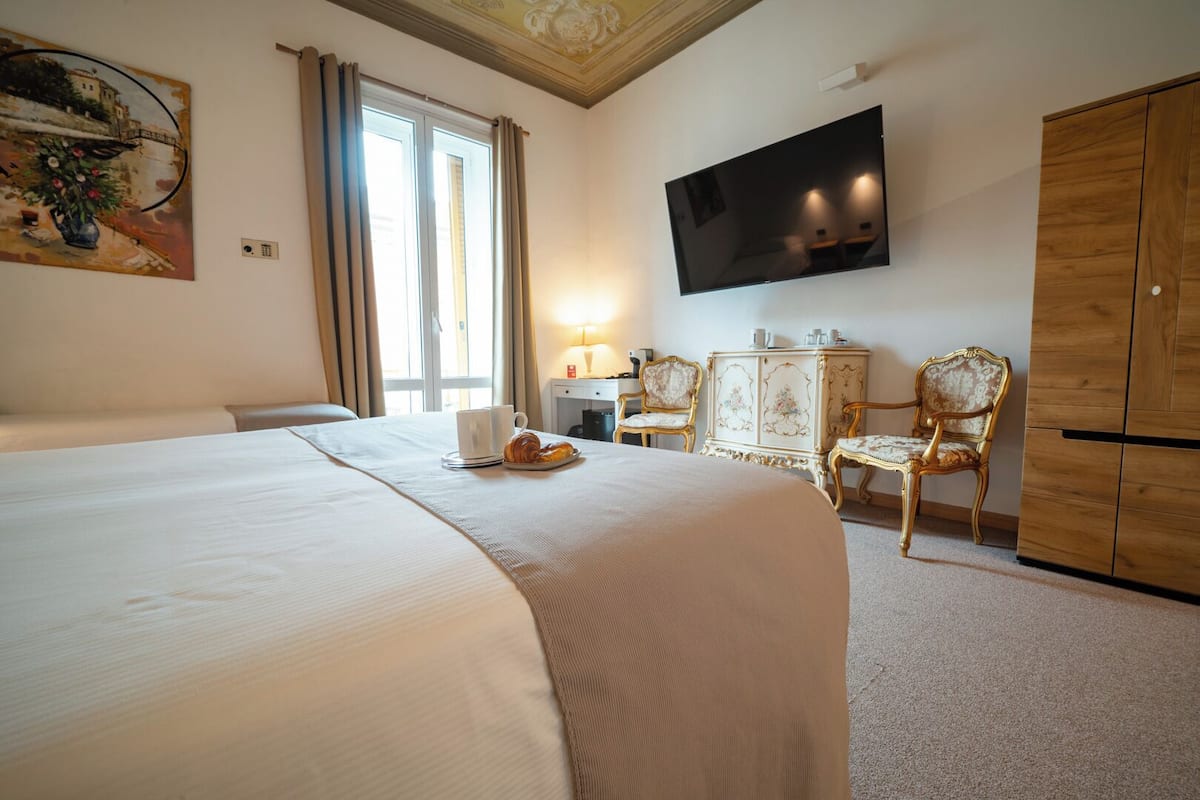 Quarto de hotel com uma cama grande, televisão de tela plana, guarda-roupa de madeira e escrivaninha com abajur.