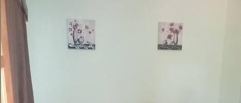 Uma sala de estar com um sofá preto, uma mesa de centro de madeira e uma poltrona estampada. Há duas pinturas penduradas na parede acima do sofá.