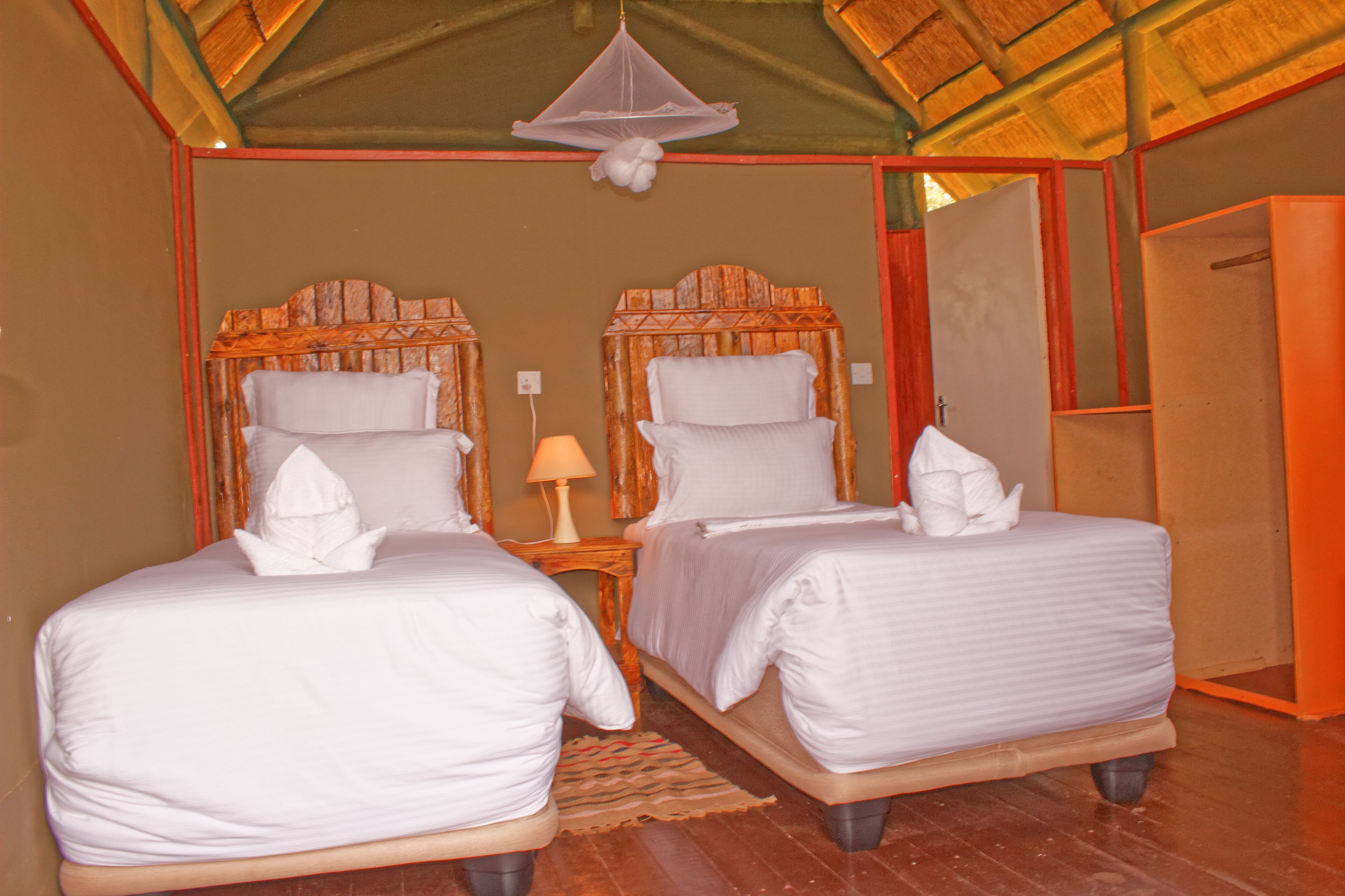 Quarto com duas camas, cabeceiras de madeira, mosquiteiro suspenso e piso de madeira.