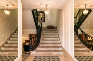 Uma escadaria imponente com corrimão preto, um candelabro e um piso estampado.