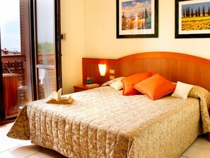 Quarto de hotel com cama, mesa de cabeceira, luminária e janela com vista para o mar.