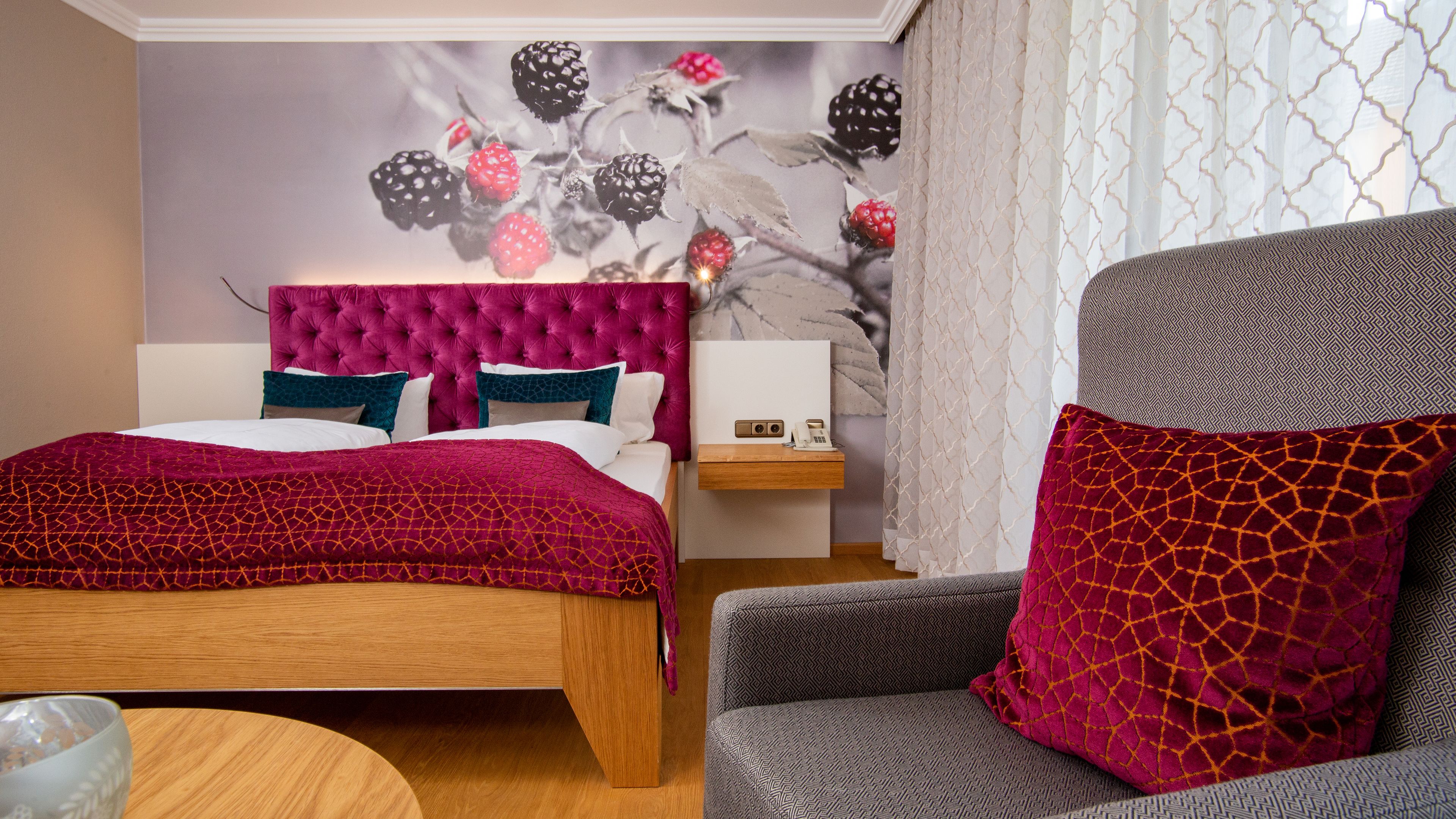 Quarto de hotel com uma cama, uma cadeira, uma mesa de cabeceira e um mural na parede.