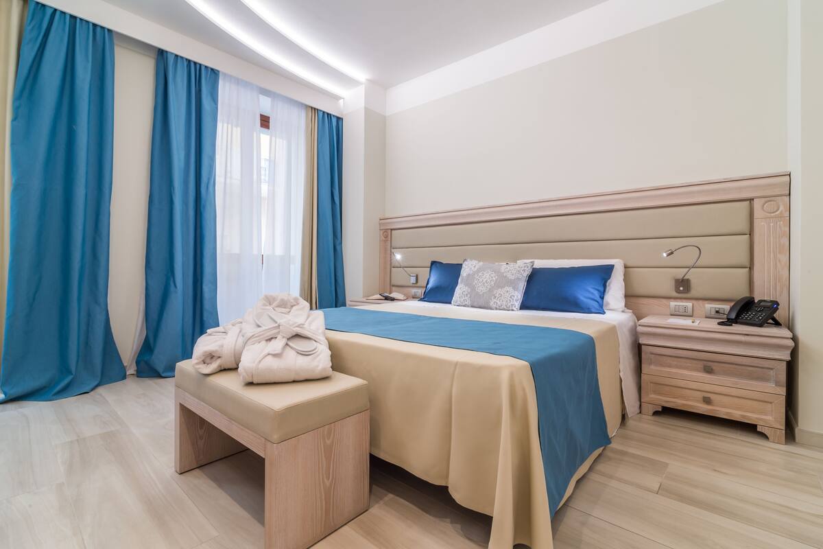 Quarto de hotel com cama, mesa de cabeceira e um banco.