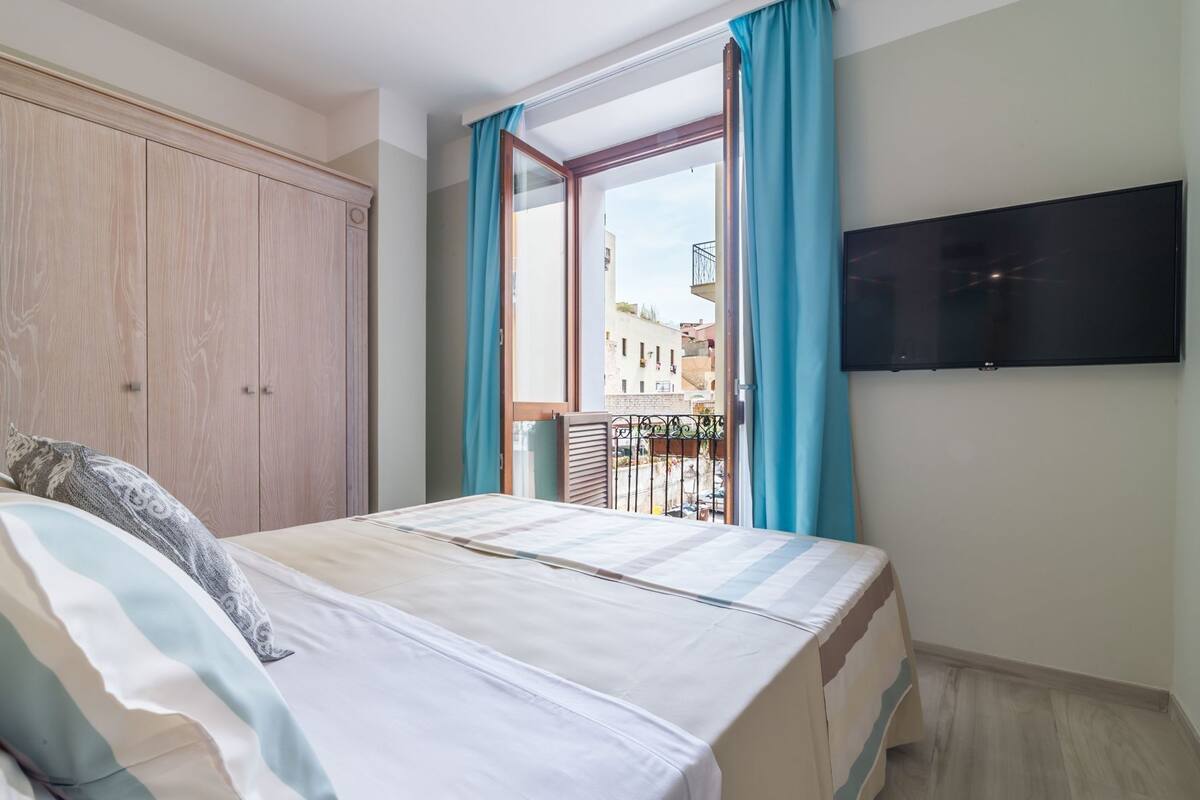 Quarto com uma cama, televisão, guarda-roupa e janela com cortinas.