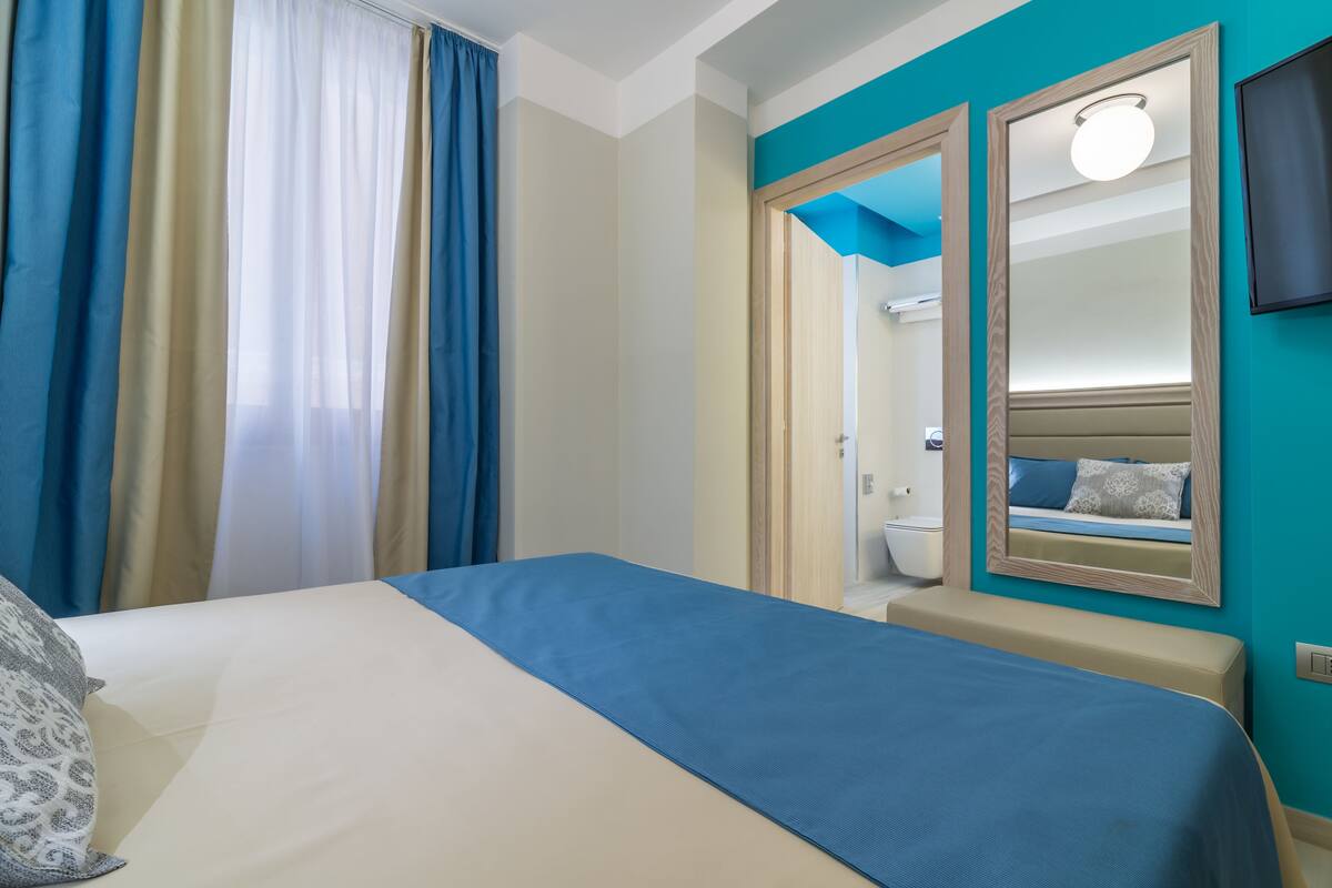 Quarto de hotel com cama, espelho e vista para o banheiro.