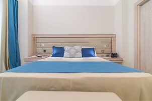 Quarto de hotel com cama, mesa de cabeceira, telefone e abajur.