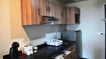 Uma cozinha compacta com armários de madeira, bancada preta, torradeira, chaleira e lava-louças.