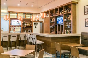 Uma área de bar com diversas opções de assento, uma tela de televisão e uma variedade de garrafas de bebidas.