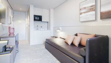 Uma sala de estar moderna com sofá, mesa de centro, luminária e área de cozinha com armários e micro-ondas.