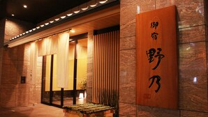 Entrada de hotel com uma placa de madeira exibindo caracteres chineses, piso de azulejos e uma entrada tradicional no estilo japonês com portas deslizantes.