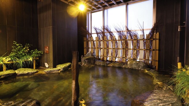 Uma onsen japonesa tradicional com uma banheira de pedra, cercada por bambu e rochas.