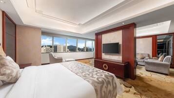 Quarto de hotel com uma cama grande, televisão, sofá e vista para a paisagem urbana.