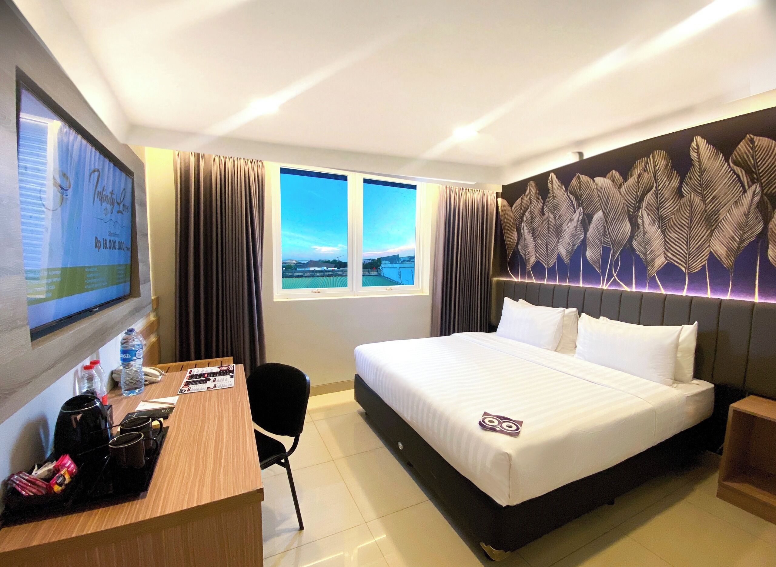 Quarto de hotel com cama, escrivaninha com cadeira, televisão e vista para o mar através de duas janelas.