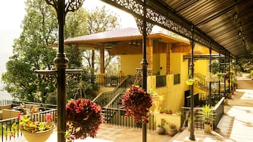 Um espaço ao ar livre coberto com uma escadaria que leva a um edifício amarelo, rodeado por vasos de plantas e cestos suspensos com flores.