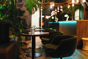 Interior de restaurante com mesas redondas, cadeiras estofadas verdes e luminárias pendentes.