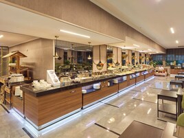 Um saguão de hotel moderno com um longo balcão de buffet, área de estar e um chefe preparando alimentos.