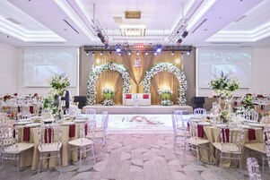 Uma sala de banquetes com palco, fileiras de mesas e cadeiras.
