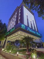 Um hotel com fachada moderna, letreiros iluminados e área de entrada ajardinada.
