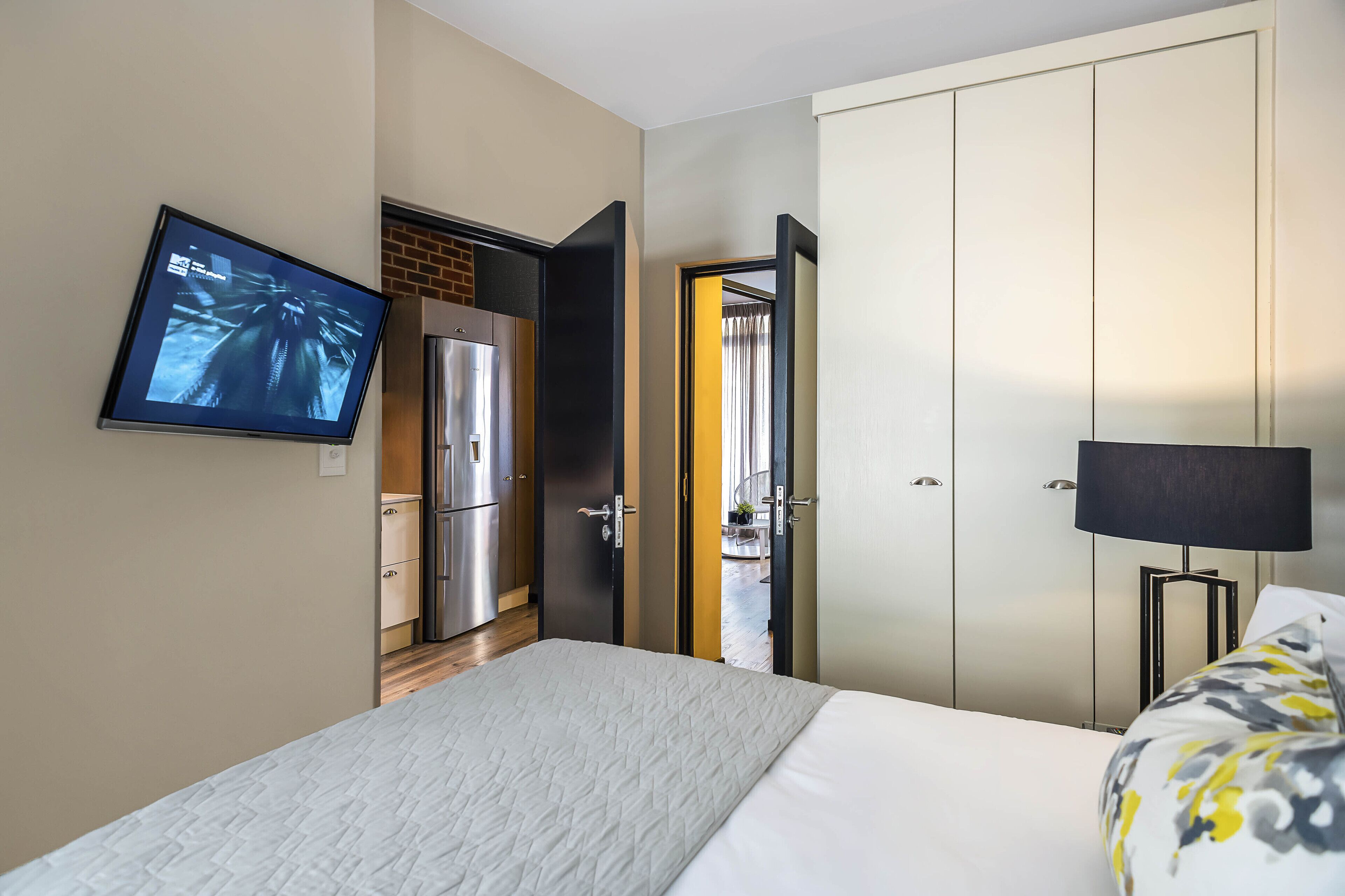 Quarto de hotel com cama, televisão fixada na parede, frigorífico e guarda-roupa.