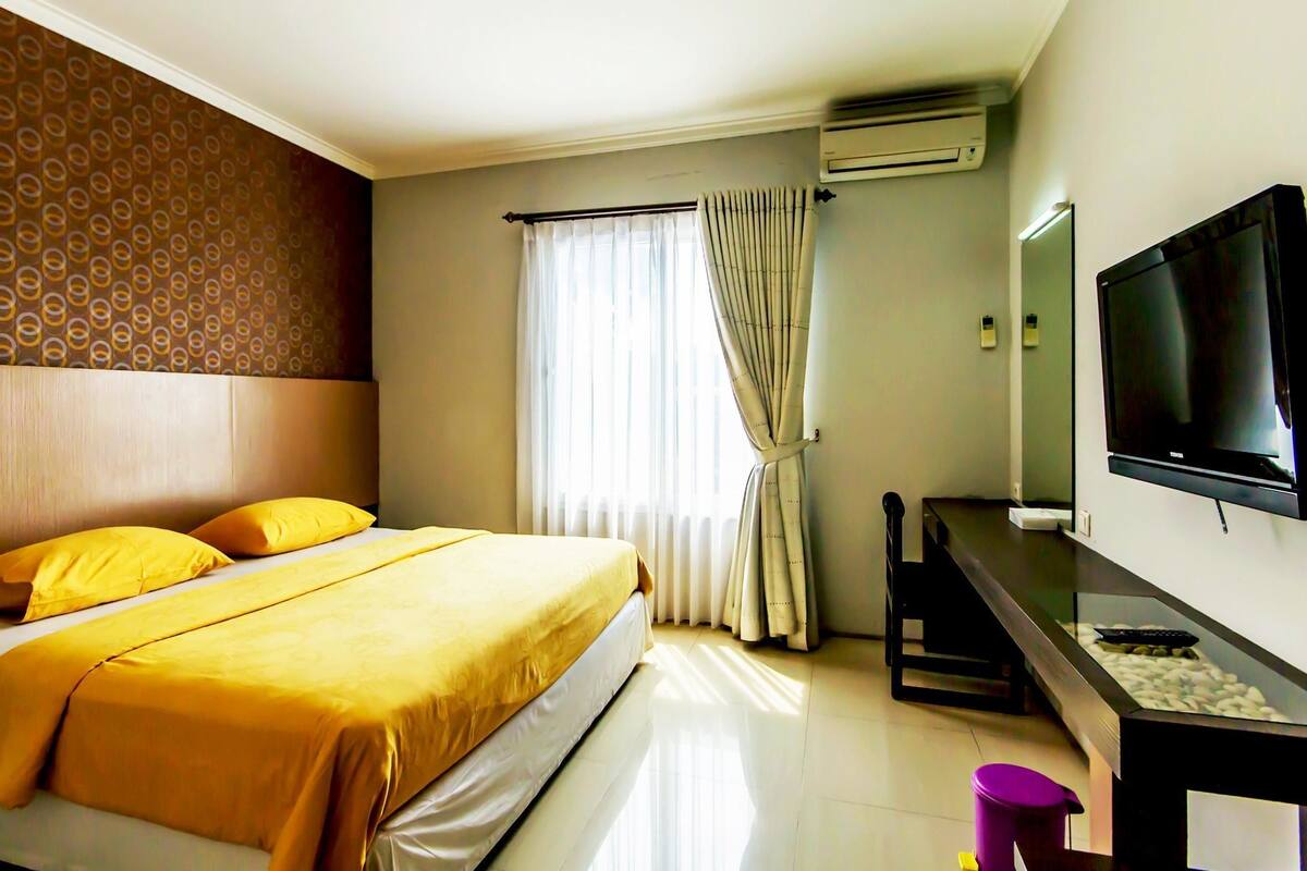 Quarto de hotel com cama, televisão, ar condicionado e janela com cortinas.