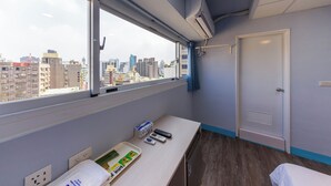 Quarto de hotel com vista para a cidade, uma mesa com controles remotos, uma cama e uma porta.
