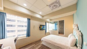 Quarto de hotel com cama, escrivaninha, cadeira, televisão e banheiro com chuveiro.