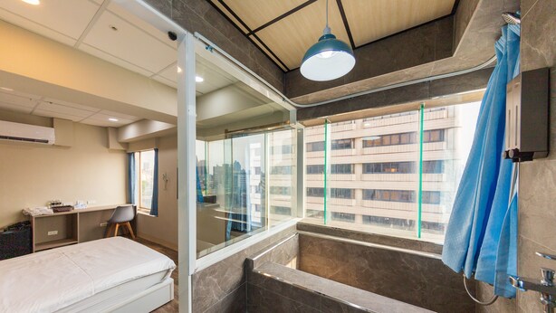 Quarto de hotel moderno com cama, escrivaninha e uma janela grande com vista para a cidade.