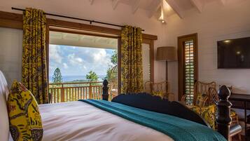 Quarto com cama grande, varanda com cortinas, área de refeições com cadeiras e televisão na parede.