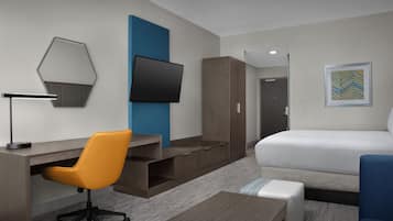 Quarto de hotel com cama, escrivaninha, cadeira, televisão e guarda-roupa.