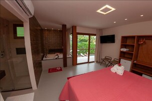 Quarto de hotel com uma cama grande, chuveiro, TV e vista para o exterior.