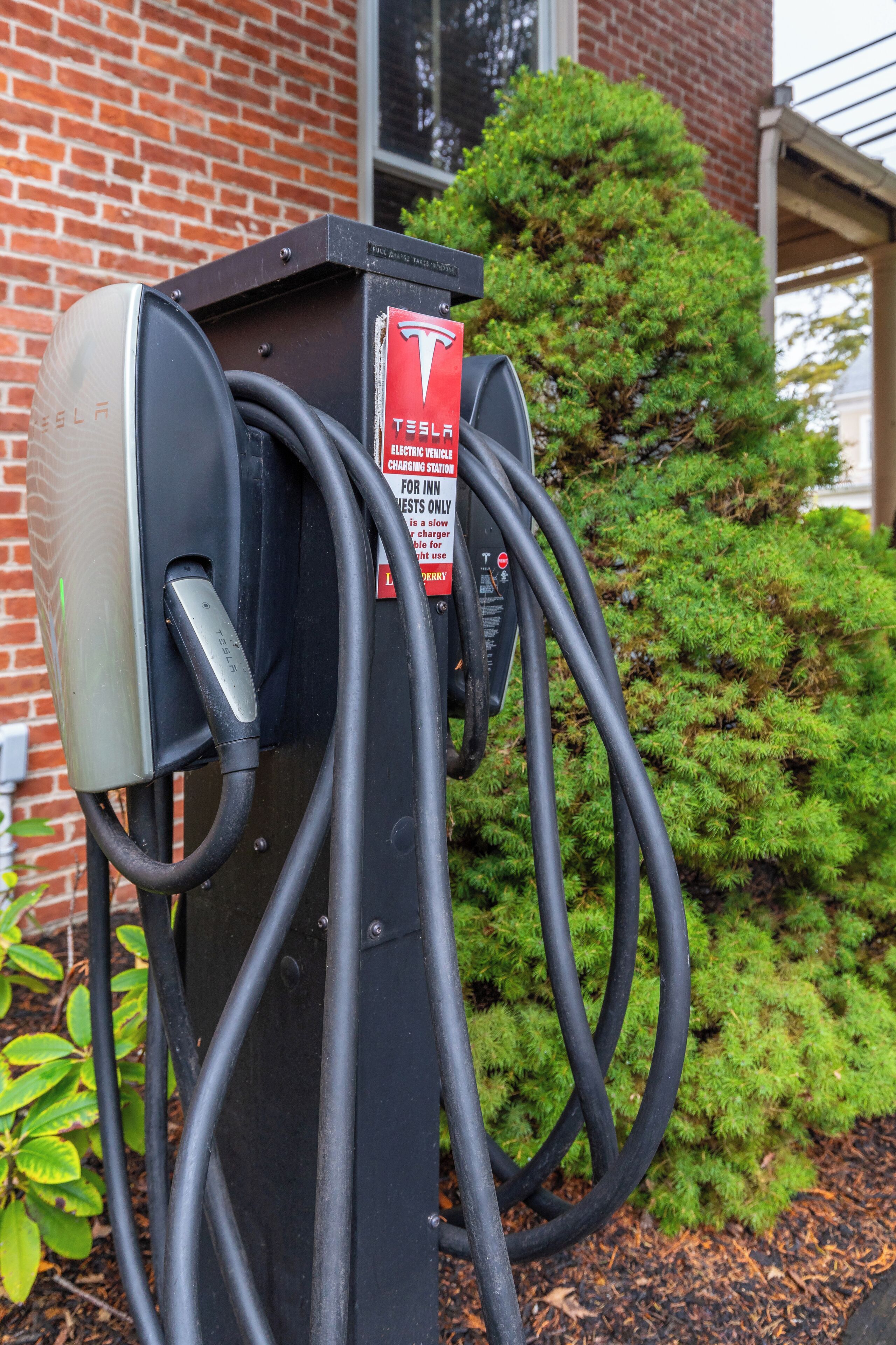 Estação de carregamento para veículos elétricos Tesla, com vários cabos de carregamento, o logotipo Tesla e uma placa indicando que é exclusiva para hóspedes da rede.